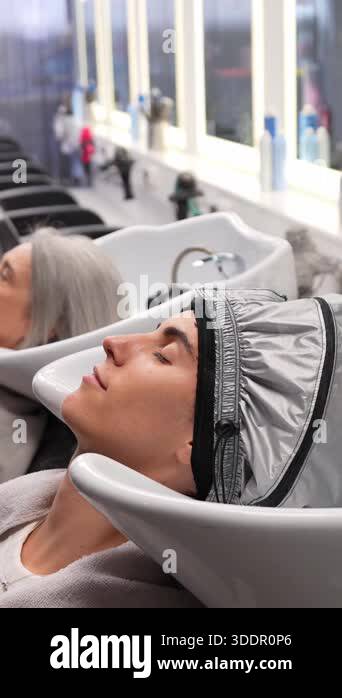 Man with closed eyes relaxing in a sink at a hair salon. A thermal cap ...