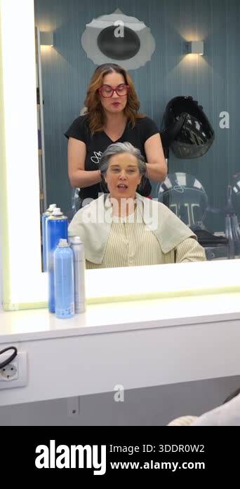 Smiling professional hairstylist creating a new hairstyle for a mature ...
