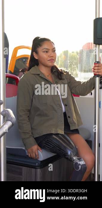 Beautiful young woman with a leg prosthesis standing up on a public bus ...