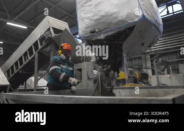 Worker cuts industrial bulk bag releasing rubber material into shredder ...