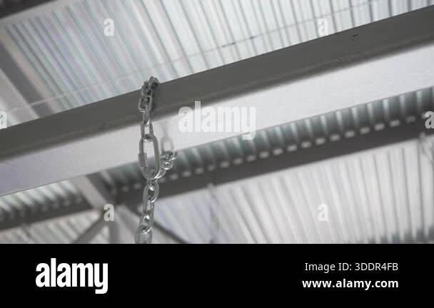 Metal chain mount hangs from beam beneath tall industrial ceiling ...