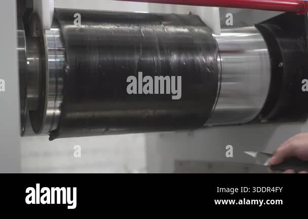 Worker cuts asymmetric rubber sheet from rotating recycled rubber ...