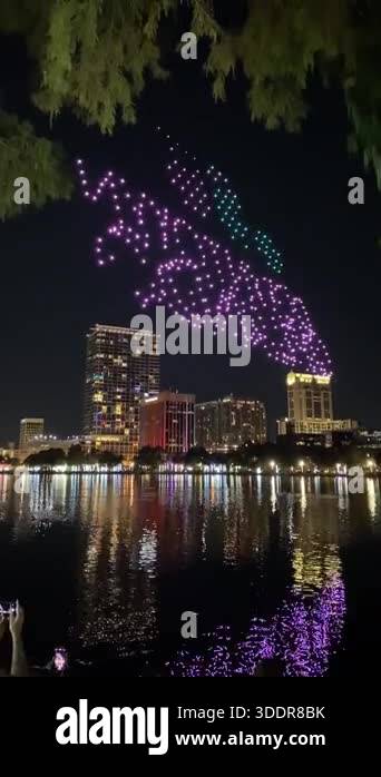 A colorful drone light show glows above a modern city skyline at night ...