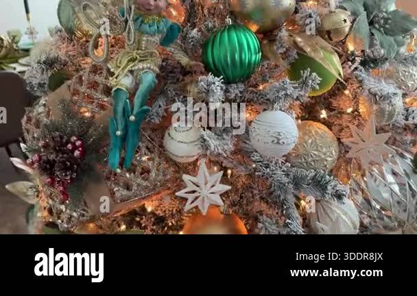 A whimsical elf doll sits on a flocked Christmas tree surrounded by ...