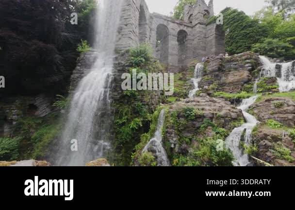Towering Waterfall Beside Ivy Covered Ruins With Archways And Mossy ...