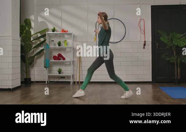 A young woman in athletic attire performs lunges with claps above her ...