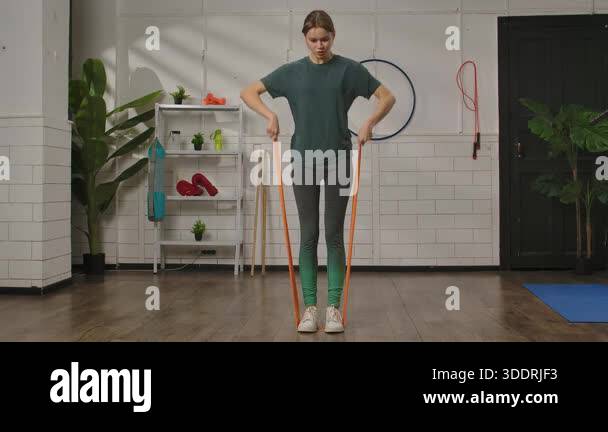 A woman performs exercises with an orange resistance band in a home gym ...