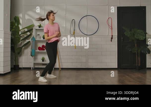 A woman in sportswear performs a long jump exercise in a gym with ...