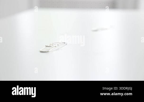 Large silver paper clips falling onto a white tabletop in a bright ...