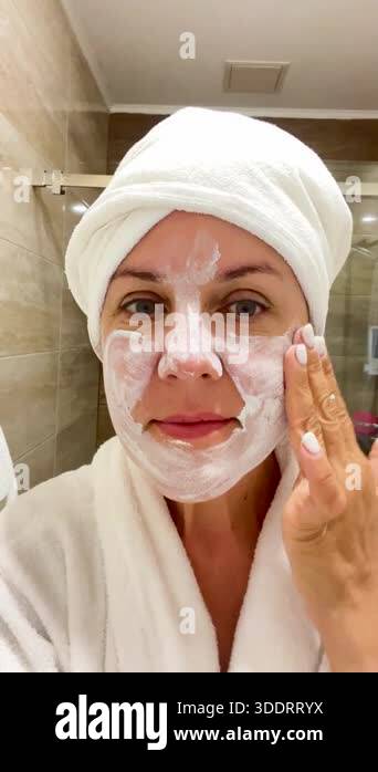 A young woman in the bathroom, in a white bathrobe and a towel on her ...