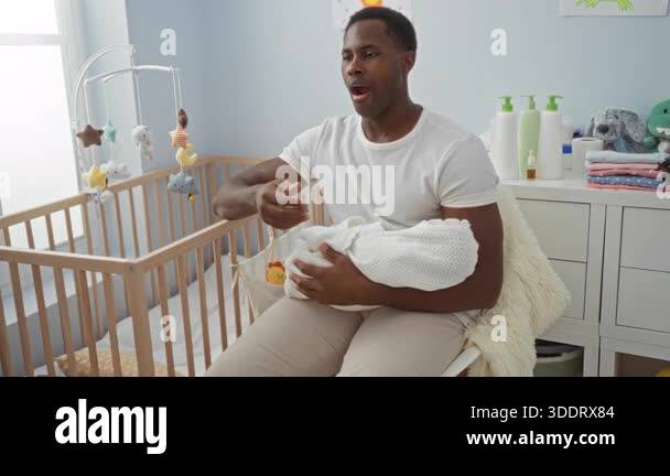 Young man holding baby in bedroom, yawning while seated near wooden ...