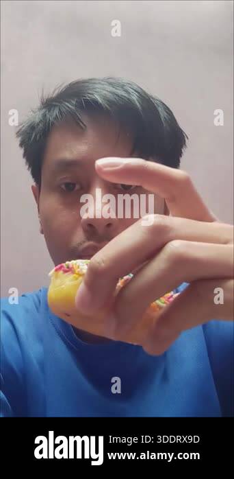 Close-up video of a man eating a donut sprinkled with colorful ...