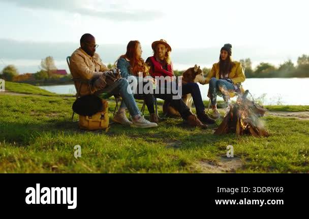 Portrait hipster friends sitting near campfire in nature. Young people ...