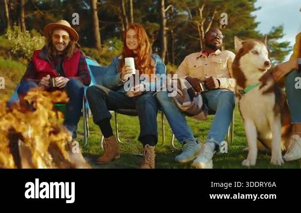 Funny friends sitting near campfire in nature. Young people talk plays ...
