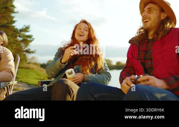 NEW YORK - April 5, 2020: Smiling friends sitting near campfire in ...