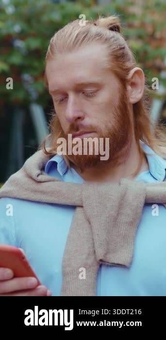A man sporting a striking red beard is checking his phone, appearing ...