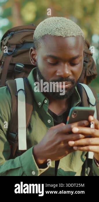 A man with a backpack checks his smartphone while enjoying nature ...