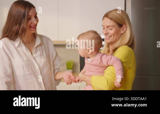 Two smiling moms talking and enjoying time with baby indoors. Lgbt ...