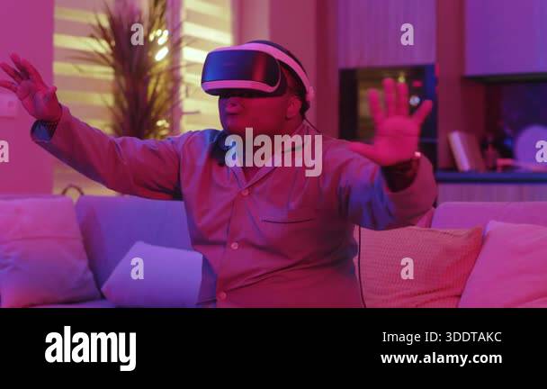 Cute mixed race young man wearing virtual reality headset sitting on ...