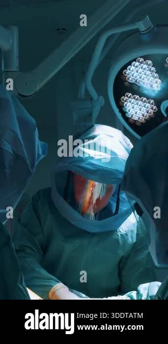 Surgeon in a protective hood working under a bright, high-tech surgical ...