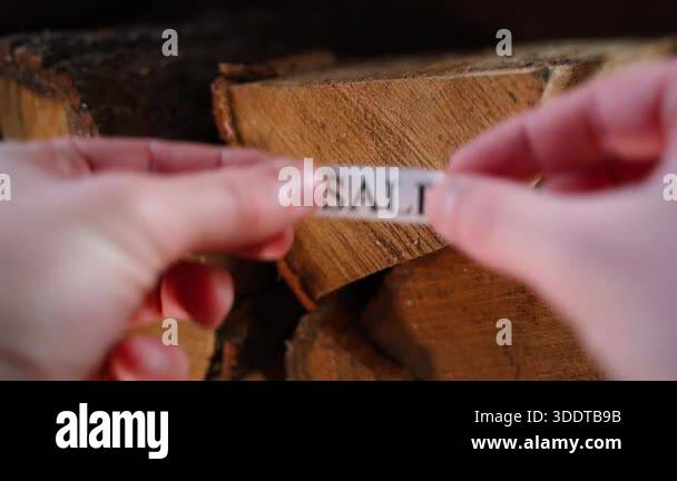 A sticker with the word SALE is being glued to firewood, close-up ...