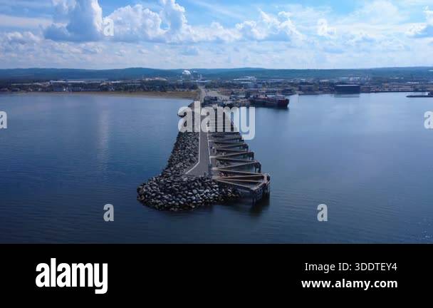A long stone jetty juts out into a tranquil bay, connecting the shore ...