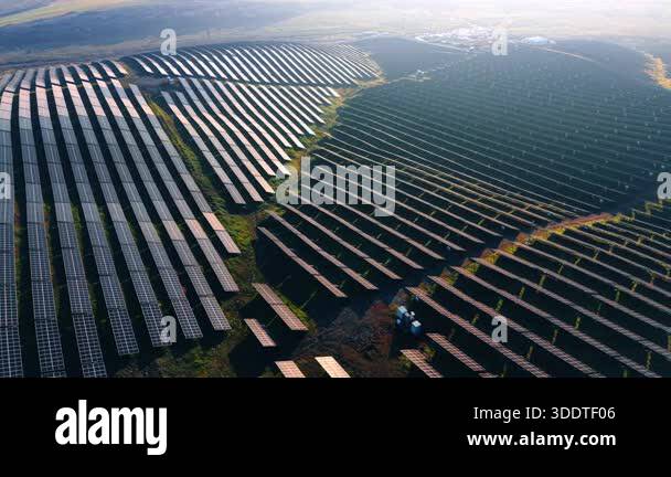 Solar panels are installed in neat rows across a hillside. It is late ...