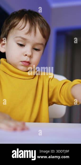 Beautiful toddler boy sits at desk drawing. Cheerful baby raises hands ...