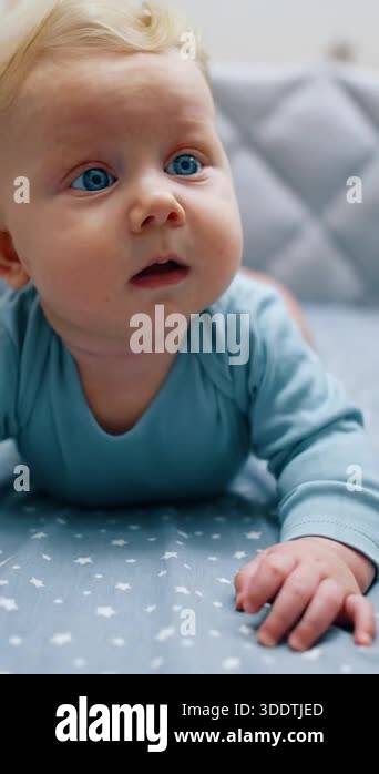 Blonde baby boy in blue clothes lies on belly leaning on his hands ...