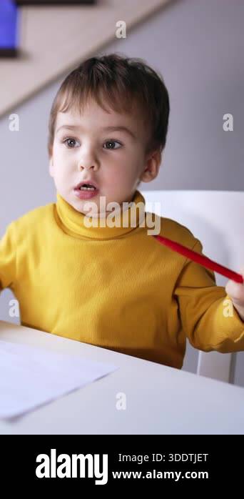 Small toddler in yellow sweater sitting at desk. Kid holds a red pen ...