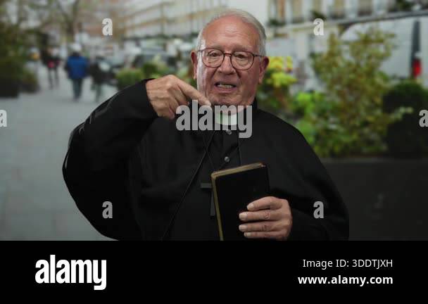 Elderly priest pointing at bible on bustling street with greenery and ...