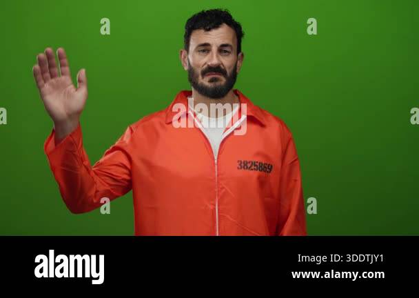 Hispanic man with beard in orange prison jumpsuit stands against green ...