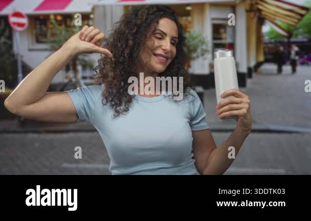 Woman holding white water bottle and points thumb to herself on busy ...