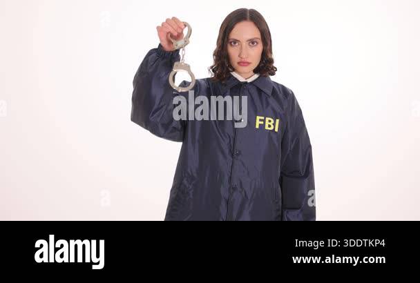 Woman agent in FBI jacket stands in studio holding metal handcuffs up ...