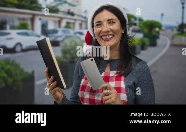 Smiling woman in red check apron and santa hat holds cleaver and book ...