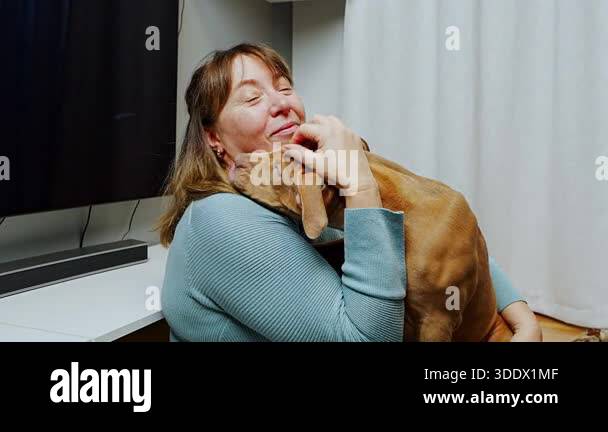Cheerful woman sitting on sofa at home, playing with her American ...