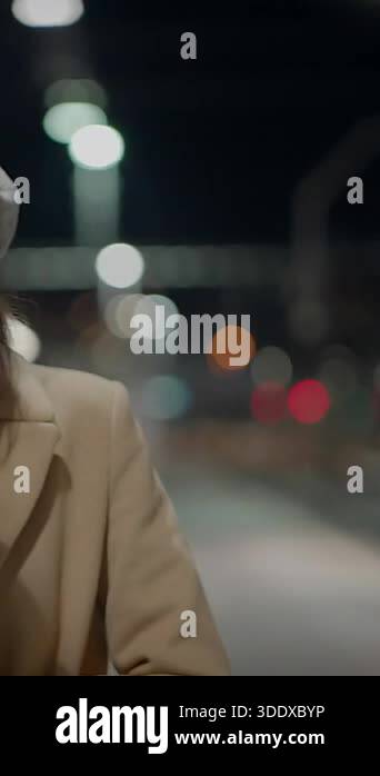 A person in a stylish outfit stands outdoors at night, talking on the ...