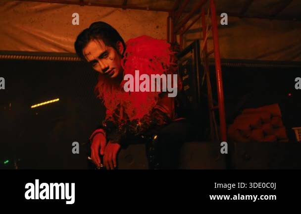 Tracking shot follows a male performer in gothic makeup and red boa ...