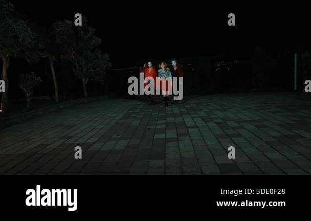 A wide shot of three people in creepy clown makeup and red and black ...