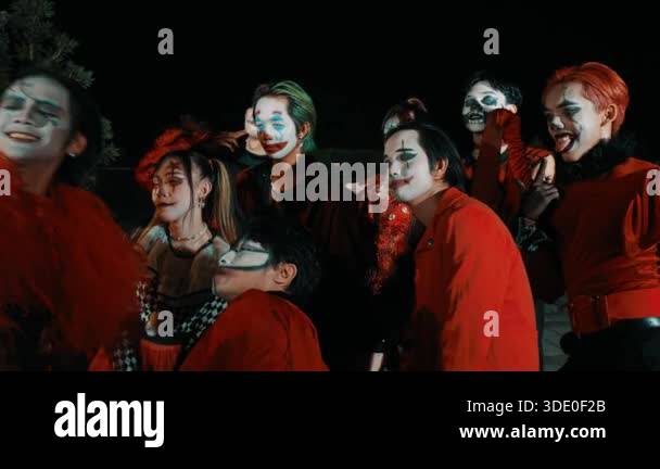 Panning shot across a group of young people in sinister clown and joker ...