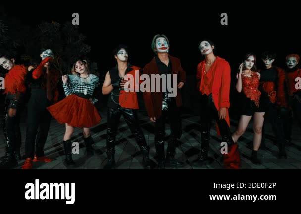 A full shot of a dance crew in horror clown costumes posing at night ...