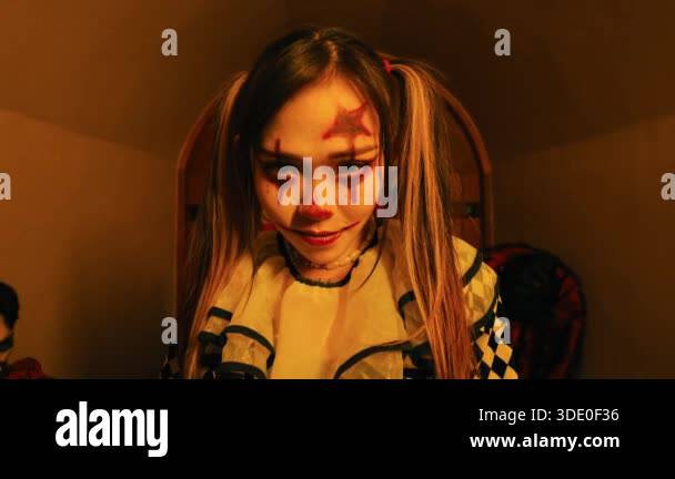 Close-up on a creepy clown girl's menacing face. She lunges forward as ...
