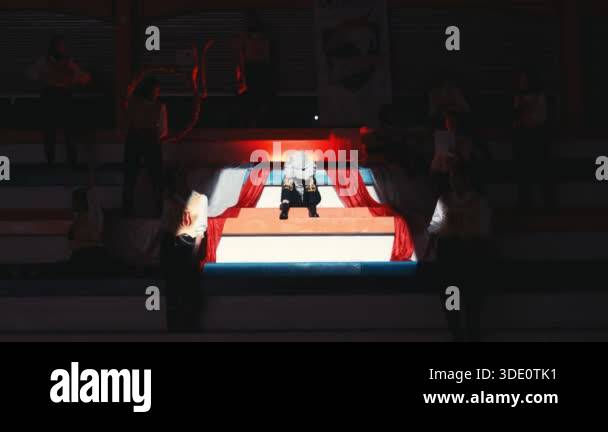 A static wide shot of a theatrical performance. A central, hooded ...