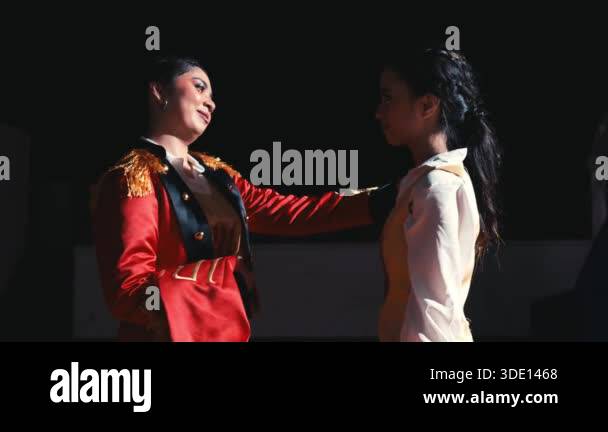 Medium shot of two women in costumes (one ringmaster) standing face-to ...