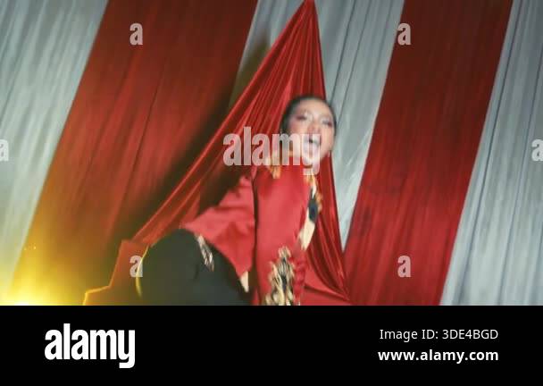 A young woman in a ringmaster costume sings expressively, dances, and ...
