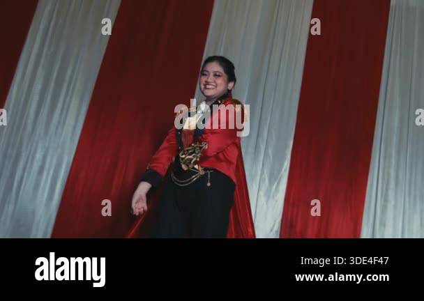 A young woman in a ringmaster outfit plays with her hair, dances on red ...