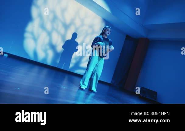 A female performer dances energetically and smiles on stage under blue ...