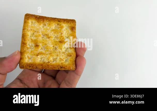 hand holding a square coconut cracker biscuit with sugar topping ...