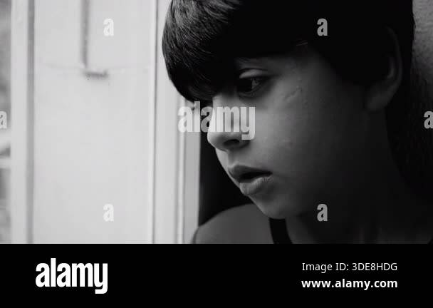 Child stands near a window with a distant look, conveying introspection ...