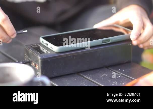 A person charging a smartphone using a portable power bank outdoors ...